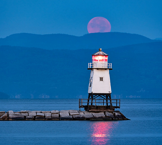 Burlington's Breakwater North Lighthouse stands sentinel against a purple twilight, while a full moon rises like nature's spotlight on this maritime guardian.