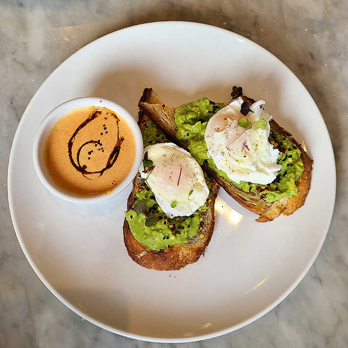 Avocado toast elevated: creamy avocado mash on artisanal bread with perfectly poached eggs and a smile drawn in the accompanying sauce.