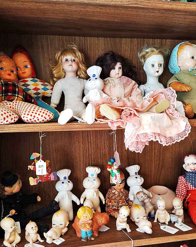 Vintage dolls with knowing eyes and delicate features line these shelves, their porcelain faces frozen in expressions that hint at the childhoods they once witnessed.