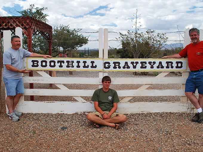 Modern visitors pose at Boothill's entrance, continuing a tradition of cemetery tourism that's somehow both morbid and delightful.