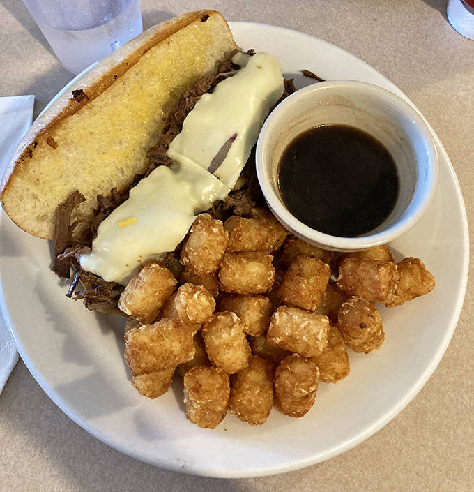 The French dip sandwich arrives with melted cheese, tender beef, and a side of au jus so good you might be tempted to drink it.