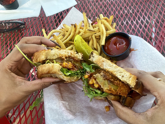 Hands eagerly unwrap this green tomato sandwich like a present &ndash; crispy, tangy, and fresh between Noble bread with fries on standby.