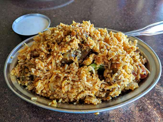 Fragrant biryani rice studded with spices and tender meat, each grain perfectly separate like tiny flavor bombs waiting to explode on your palate.
