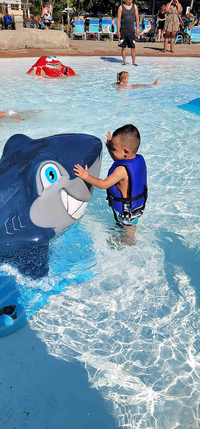 A young explorer makes friends with a smiling shark statue, proving that some of the best aquatic encounters happen on dry land.