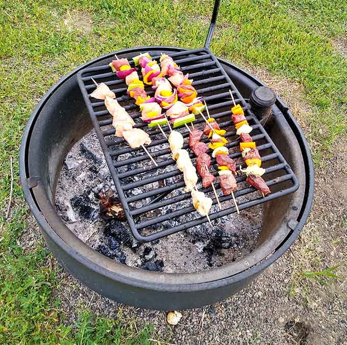 Campfire cooking elevated to an art form, where colorful skewers of meat and vegetables sizzle over flames, making everyone within smelling distance suddenly very hungry and very jealous.