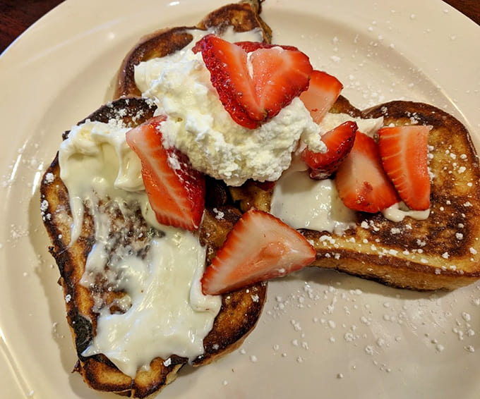 French toast done right means custardy interior meets crispy exterior, with fresh strawberries and whipped cream elevating the classic to celebration status.