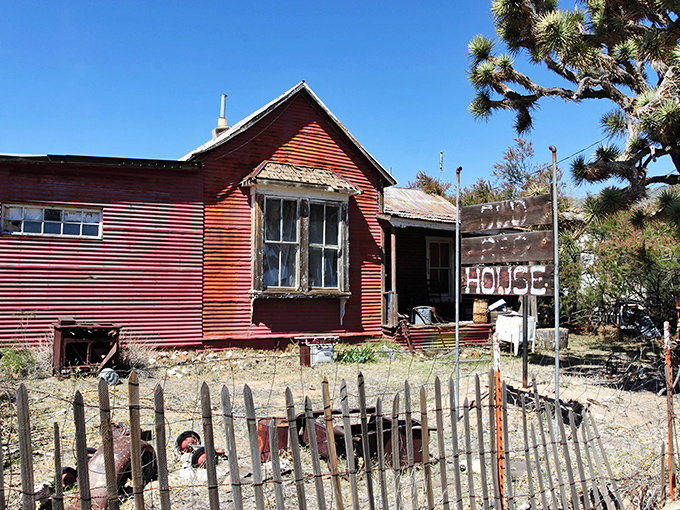 This weathered red house stands as a stubborn reminder of frontier determination, its faded walls and broken windows whispering stories of those who called it home.