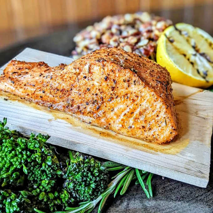 Perfectly seared salmon rests on a wooden plank like it's posing for a magazine, surrounded by vibrant greens that make healthy eating feel indulgent.