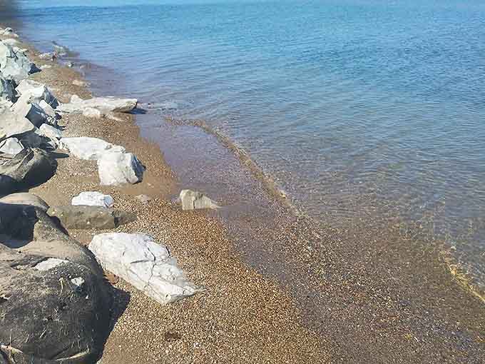 Lake Huron laps gently against the rocky shoreline, creating that soothing soundtrack of water meeting stone that beach lovers crave.