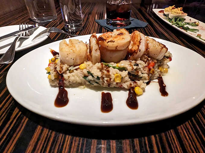 Scallops seared to golden perfection atop risotto that achieves the impossible &ndash; creamy yet perfectly al dente in every delightful bite.