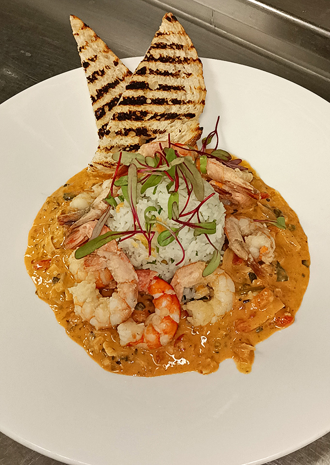 Shrimp and grits elevated to art form – plump crustaceans lounging on a bed of creamy cornmeal with triangular toast sails standing proud.