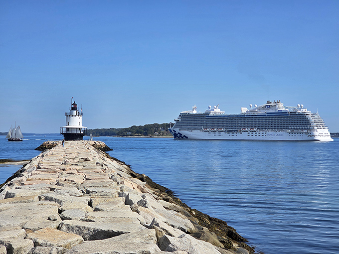 Modern meets historic as a massive cruise ship glides past the diminutive lighthouse, creating a striking contrast in maritime scales.