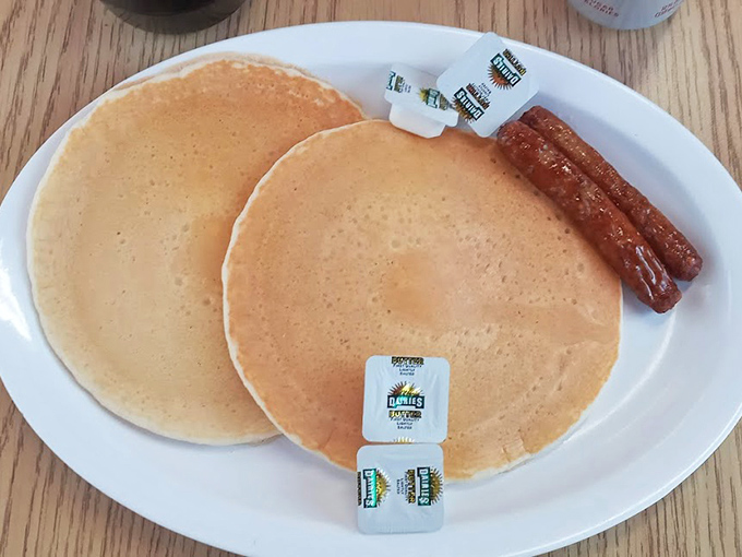 Golden pancakes with a side of sausage links – breakfast simplicity that somehow tastes better here than anywhere else. Those butter packets are about to meet their delicious destiny.
