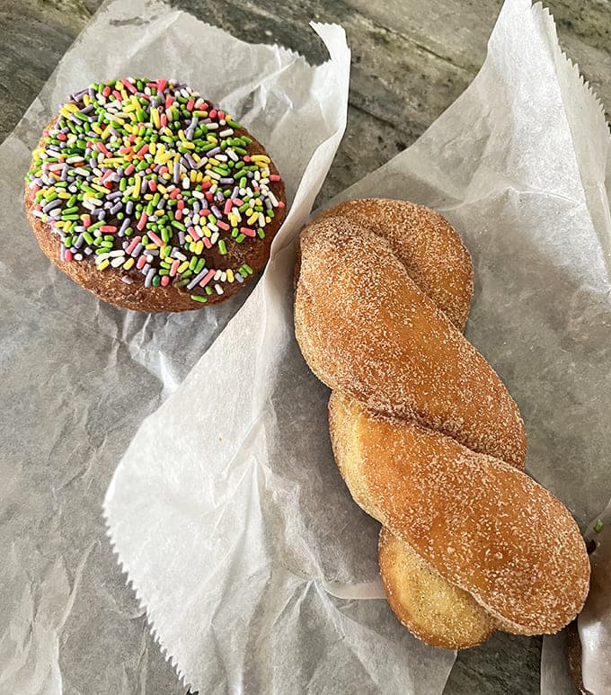 Sweet geometry: a perfectly round sprinkle-topped donut sits beside its twisted cinnamon sugar cousin &ndash; two different shapes delivering the same sugar-dusted happiness.
