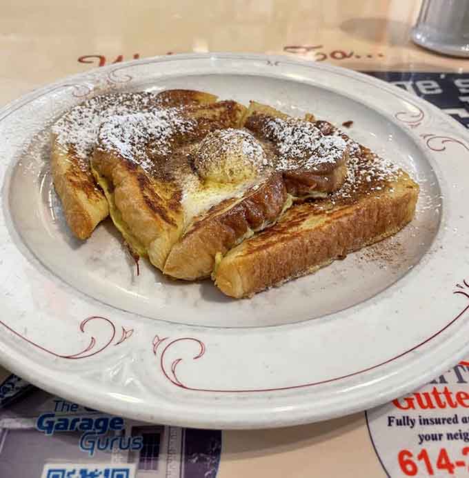 French toast arrives thick-cut and golden, dusted with powdered sugar like it's dressed up for a special breakfast occasion.