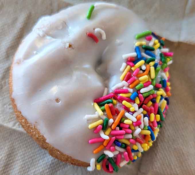 Half-dipped in vanilla glaze with a rainbow sprinkle party on one side &ndash; proof that donuts understand balance.