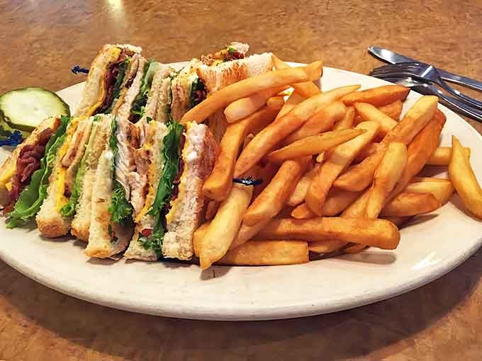 Triple-decker sandwich engineering with crisp bacon, fresh lettuce, and juicy chicken, flanked by a mountain of fries.