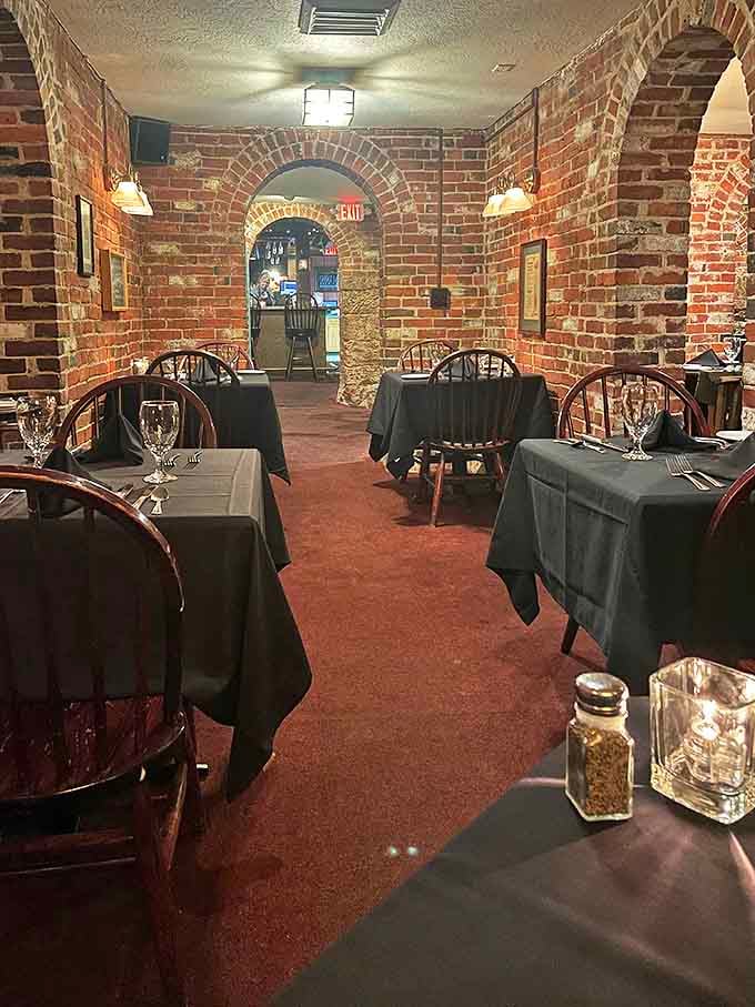 Brick archways frame intimate dining spaces where black tablecloths and wooden chairs create an atmosphere that's both historic and surprisingly cozy.