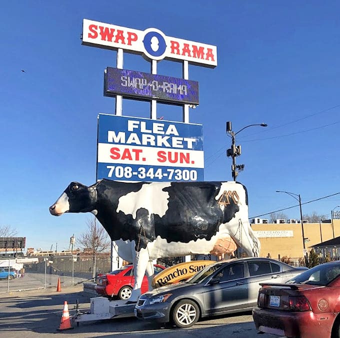 The iconic Swap-O-Rama sign with its bovine guardian &ndash; because nothing says "serious shopping" quite like a giant cow statue keeping watch.