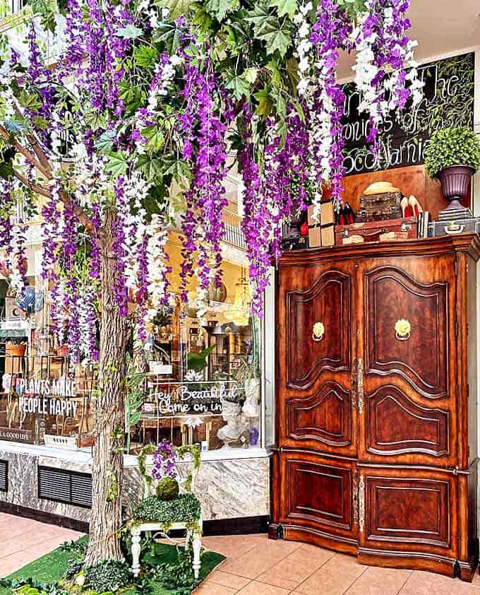 A whimsical entrance where fantasy begins &ndash; cascading purple wisteria frames an antique cabinet, promising magical moments beyond the threshold.