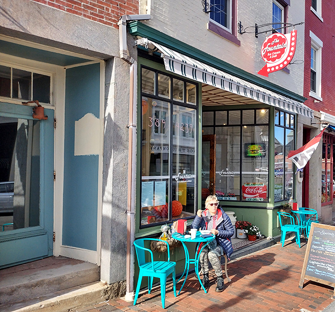 The iconic storefront of The Fountain beckons with its vintage sign and inviting turquoise tables &ndash; a slice of Americana on Bath's brick-lined Front Street.