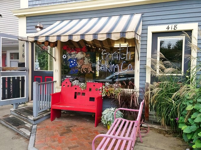 The charming exterior of Scratch Baking Co., with its inviting striped awning and signature red bench, beckons carb enthusiasts like a lighthouse for the hungry.