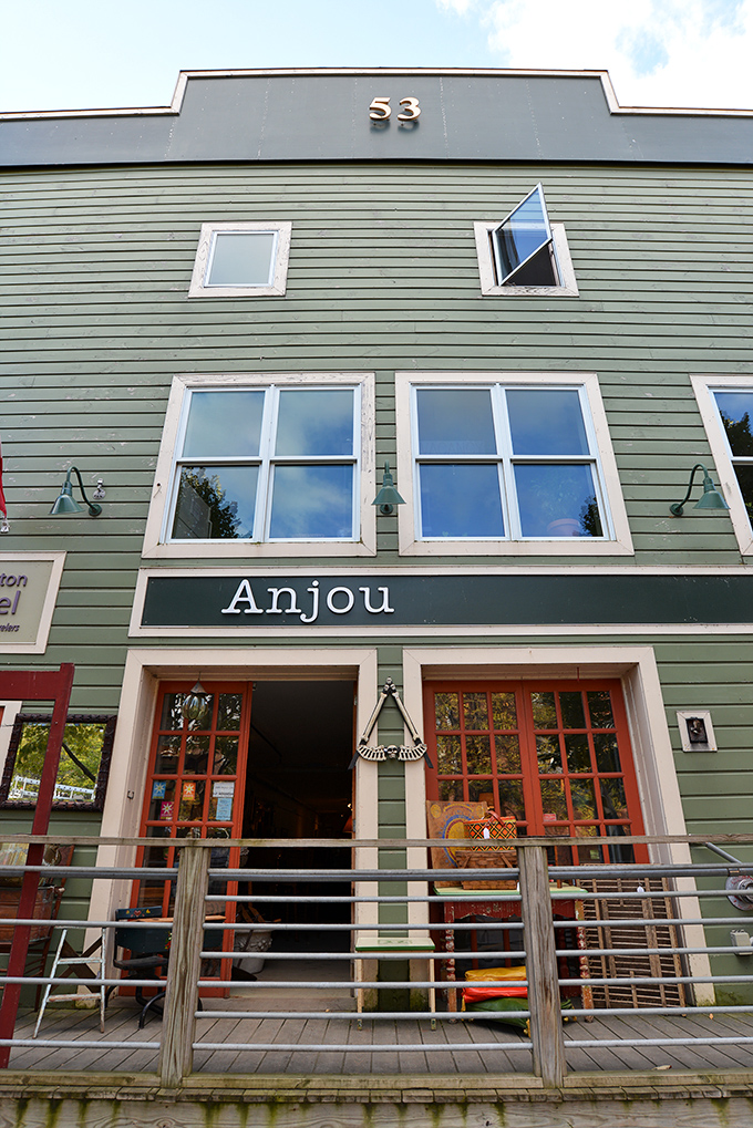 The sage-green exterior of Anjou with its welcoming red doors invites curious shoppers to discover vintage treasures within Burlington's vibrant downtown scene.