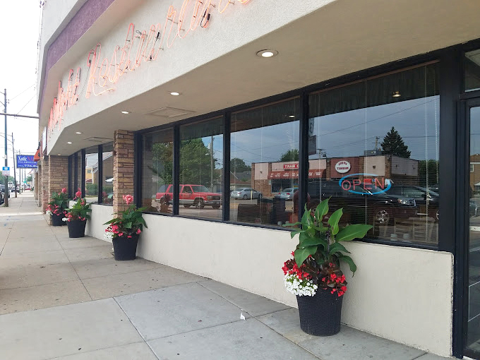 A welcoming storefront where red geraniums and morning sunshine create the perfect prelude to breakfast paradise.