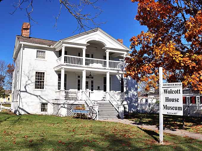 The stately Wolcott House stands proudly against a brilliant blue sky, its white clapboard and double porches whispering tales from 1827.