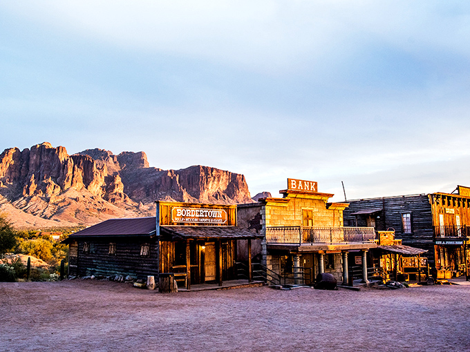 Wooden storefronts bask in golden hour light beneath the majestic Superstition Mountains – a postcard from Arizona's gold rush era perfectly preserved.