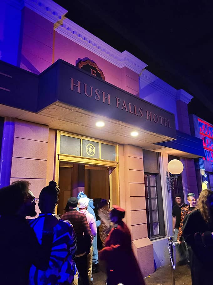 The Hush Falls Hotel entrance glows with eerie blue light, beckoning brave souls to step inside where nightmares await behind its deceptively elegant fa&ccedil;ade.
