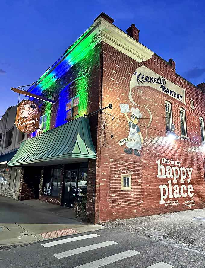 Exterior: The brick facade of Kennedy's Bakery glows with colorful lights, proudly declaring "this is my happy place" &ndash; a century-old promise kept nightly.