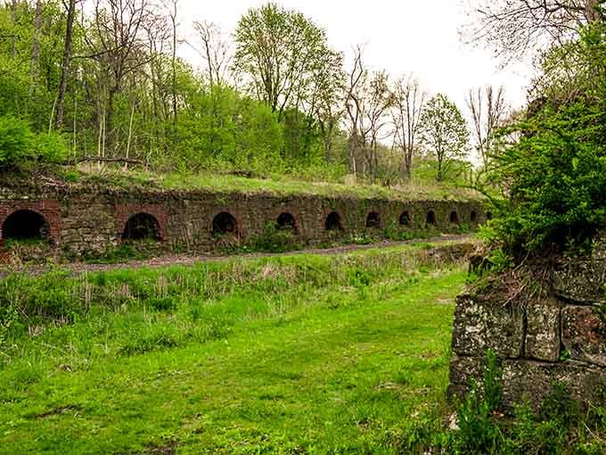 Ancient stone arches peek through lush greenery, nature's slow embrace reclaiming what industry once claimed as its own.