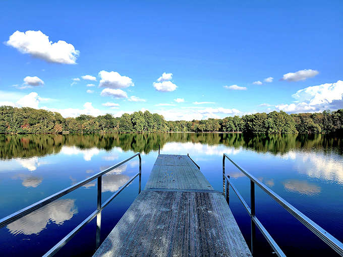 A wooden dock stretches into mirror-like waters, where sky meets lake in perfect reflection. Nature's own infinity pool.