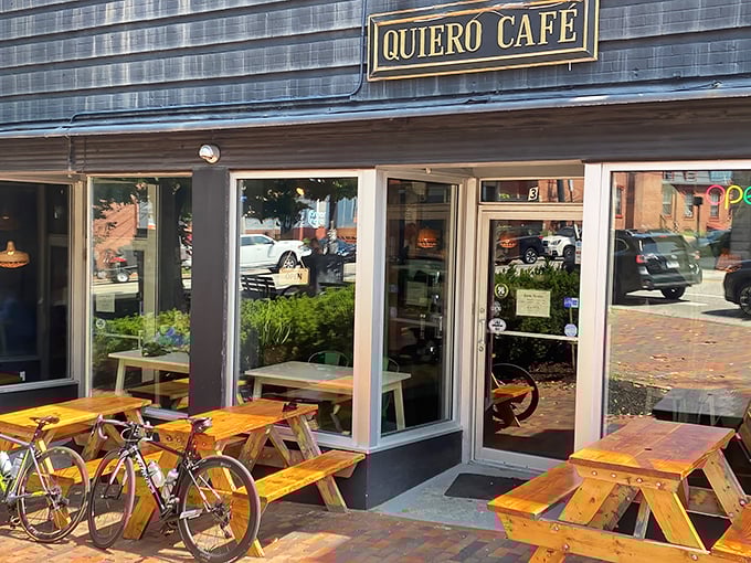 Exterior: Quiero Caf&eacute;'s charming blue-gray exterior with rustic wooden picnic tables invites passersby to pause for a Latin American flavor adventure.