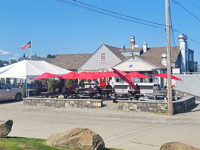 The charming exterior of Fox's Lobster House beckons with red umbrellas and waterfront views that scream "vacation mode activated."
