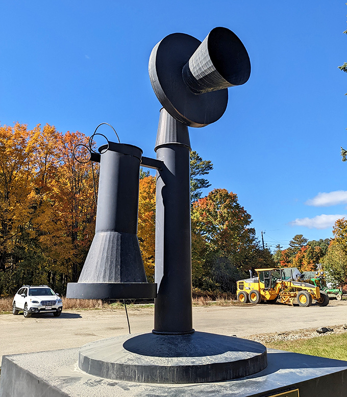 The World's Largest Telephone stands proudly against a brilliant blue Maine sky, its massive black form creating a striking silhouette among autumn foliage.