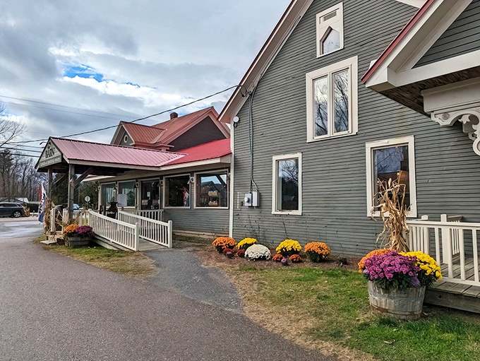 The welcoming exterior of Cold Hollow Cider Mill, where Vermont charm meets apple paradise &ndash; a gray building with red roof that practically whispers "calories don't count here."