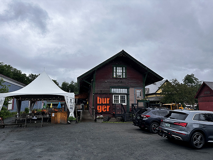 The weathered red barn exterior of Worthy Burger stands proudly alongside Vermont railroad tracks, its "burger" sign glowing like a beacon for hungry travelers.