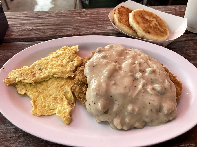 Country gravy cascades over crispy chicken fried steak like a delicious waterfall, with golden eggs standing by for breakfast perfection.