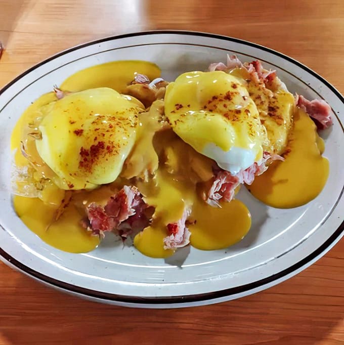 Eggs Benedict: Poached eggs perched atop ham, draped in hollandaise &ndash; a breakfast classic executed with the kind of precision that makes 3 AM decisions easy.