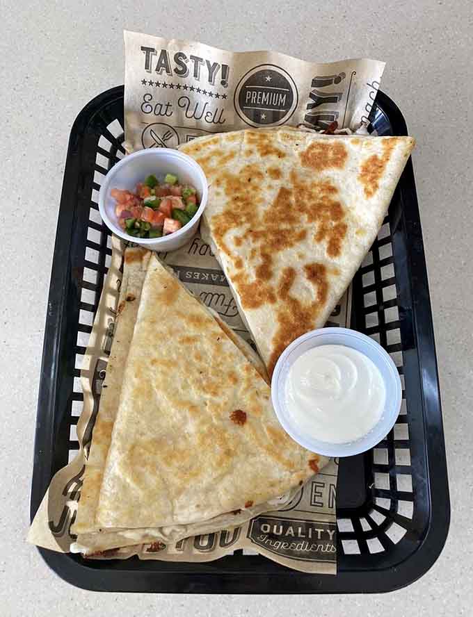 The quesadilla arrives golden and crispy, cut into manageable triangles with sides of salsa and crema for dipping and drizzling.