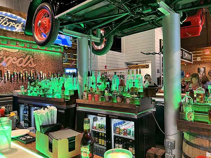The bar area glows with green lighting and features an impressive craft beer selection beneath more suspended automotive treasures.