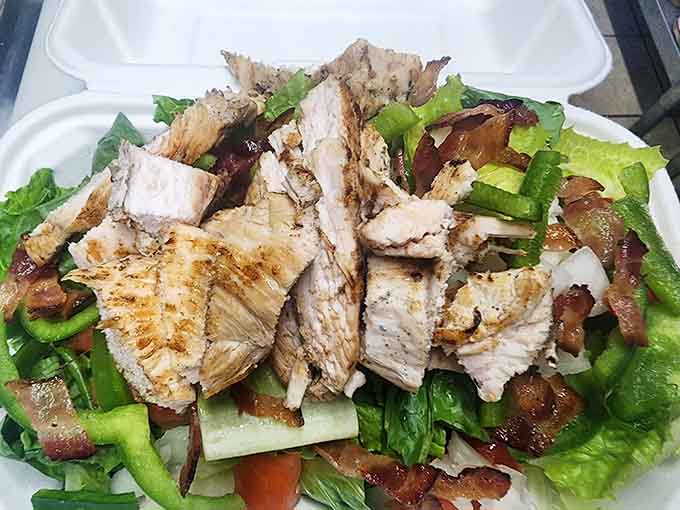 Grilled chicken tops a generous salad with bacon and fresh vegetables for those seeking lighter fare options.