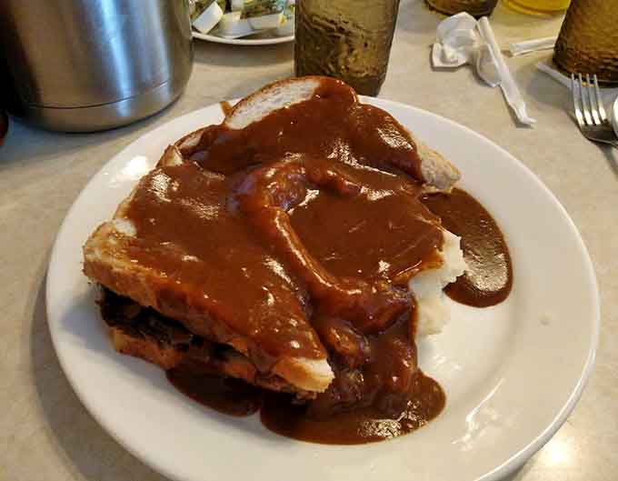 Hot beef sandwich swimming in gravy like it's training for the Olympics, comfort food that hugs you from the inside out.