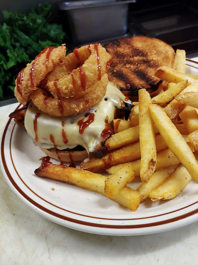 A burger that demands a two-handed commitment, topped with an onion ring crown &ndash; casual royalty on a plate of golden fries.