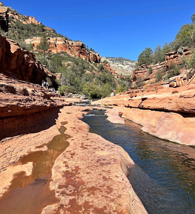 Oak Creek's crystal waters flow over smooth red stone, creating nature's own infinity pool against a backdrop of towering cliffs.