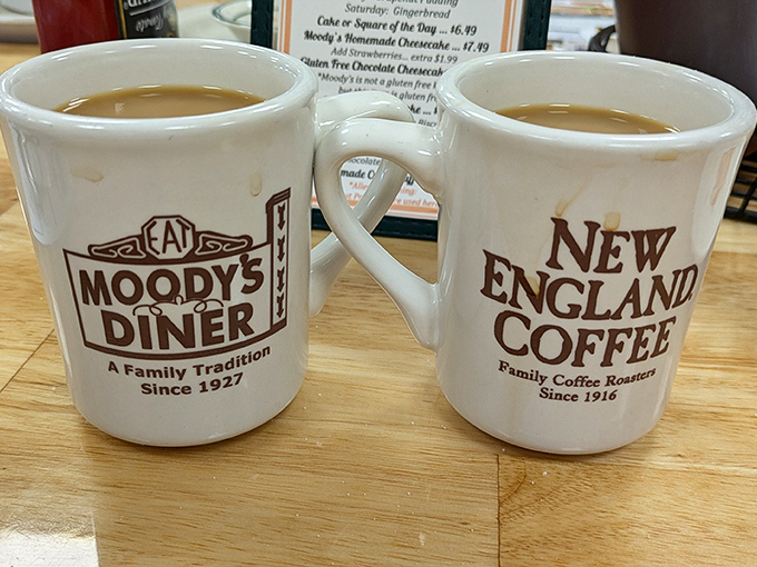 The classic New England Coffee mug sits beside Moody's own branded cup, both promising refills that keep coming.