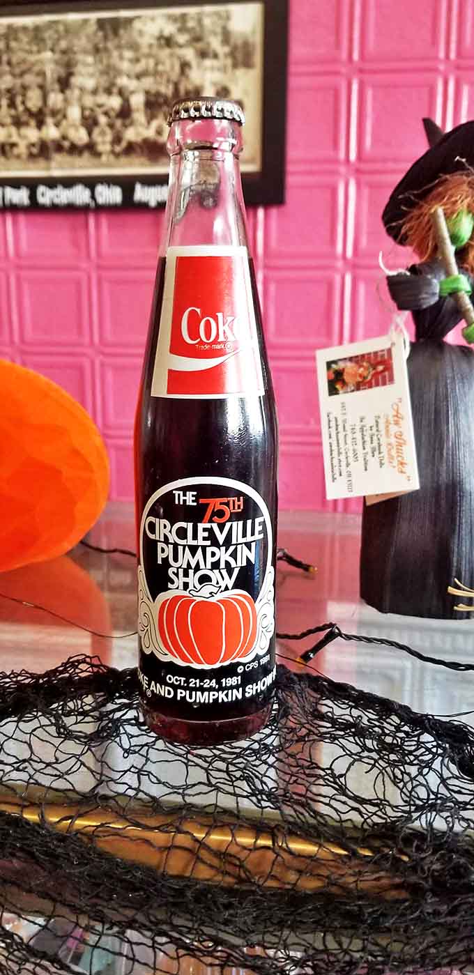 A vintage Circleville Pumpkin Show commemorative Coke bottle against pink tile &ndash; a slice of local history preserved alongside the sweet traditions.