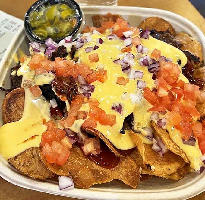 A mountain of crispy tortilla chips smothered in melted cheese, diced tomatoes, red onions, and jalape&ntilde;os &ndash; each chip becomes a treasure hunt for the perfect topping combination.
